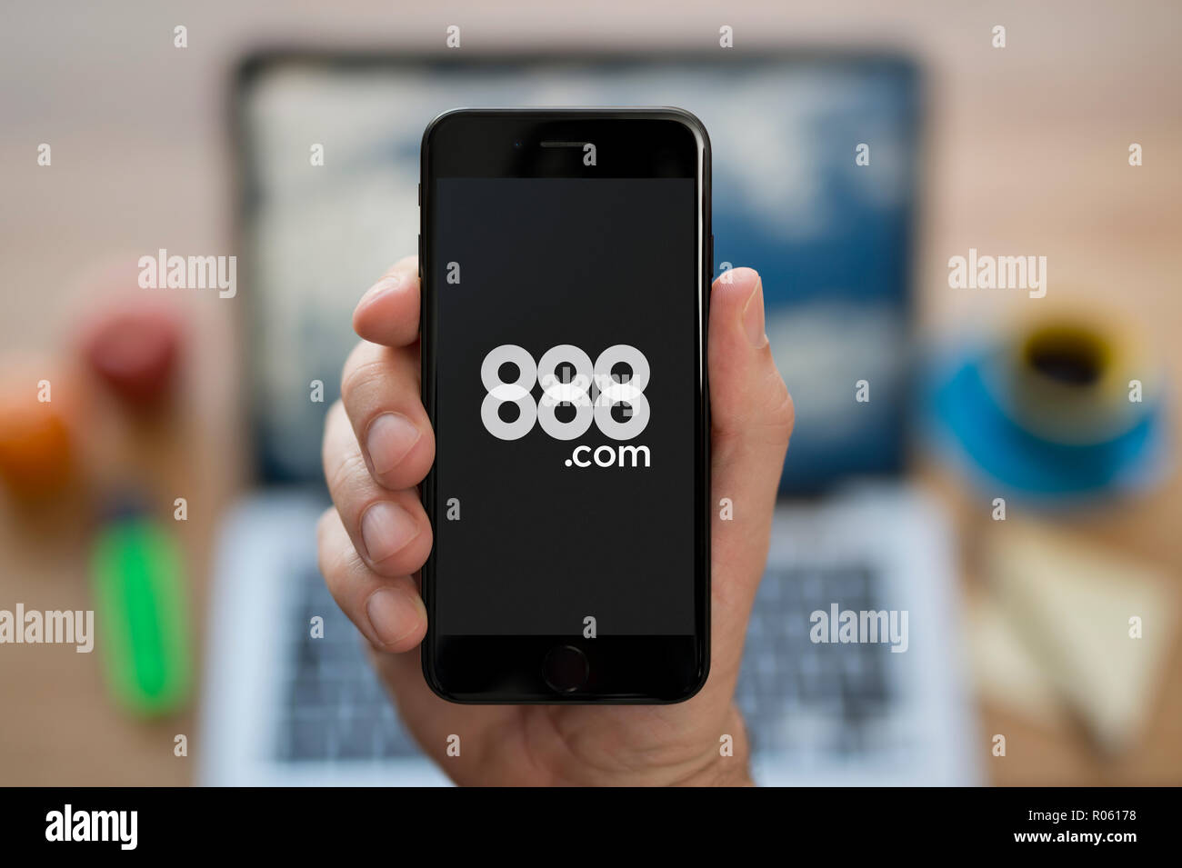 A man looks at his iPhone which displays the 888.com logo, while sat at ...