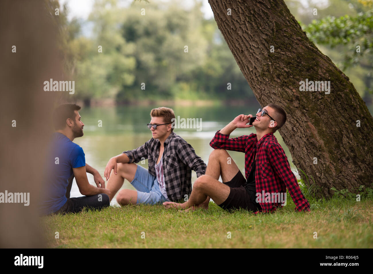 Group of young men enjoying the nature sitting on the bank of the river ...