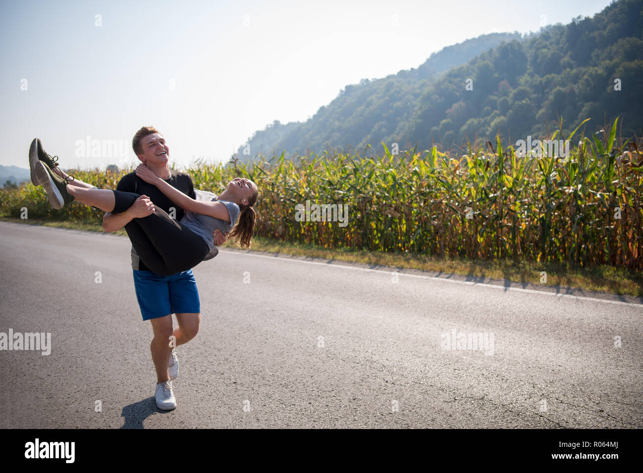 man carries a woman in his arms while jogging along a country road ...