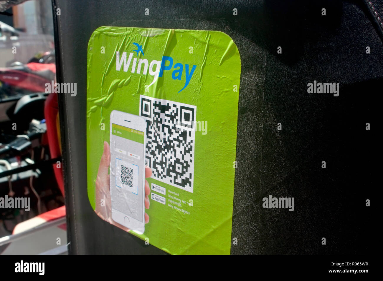 A Wing Pay mobile payment sticker is affixed to a modern taxi on a city ...