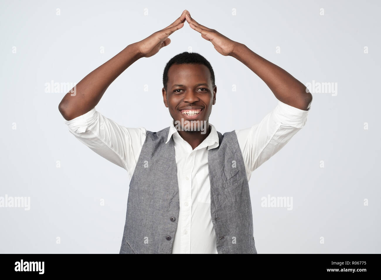 Portrait of a cheerful man holding hands over head like a roof house on ...