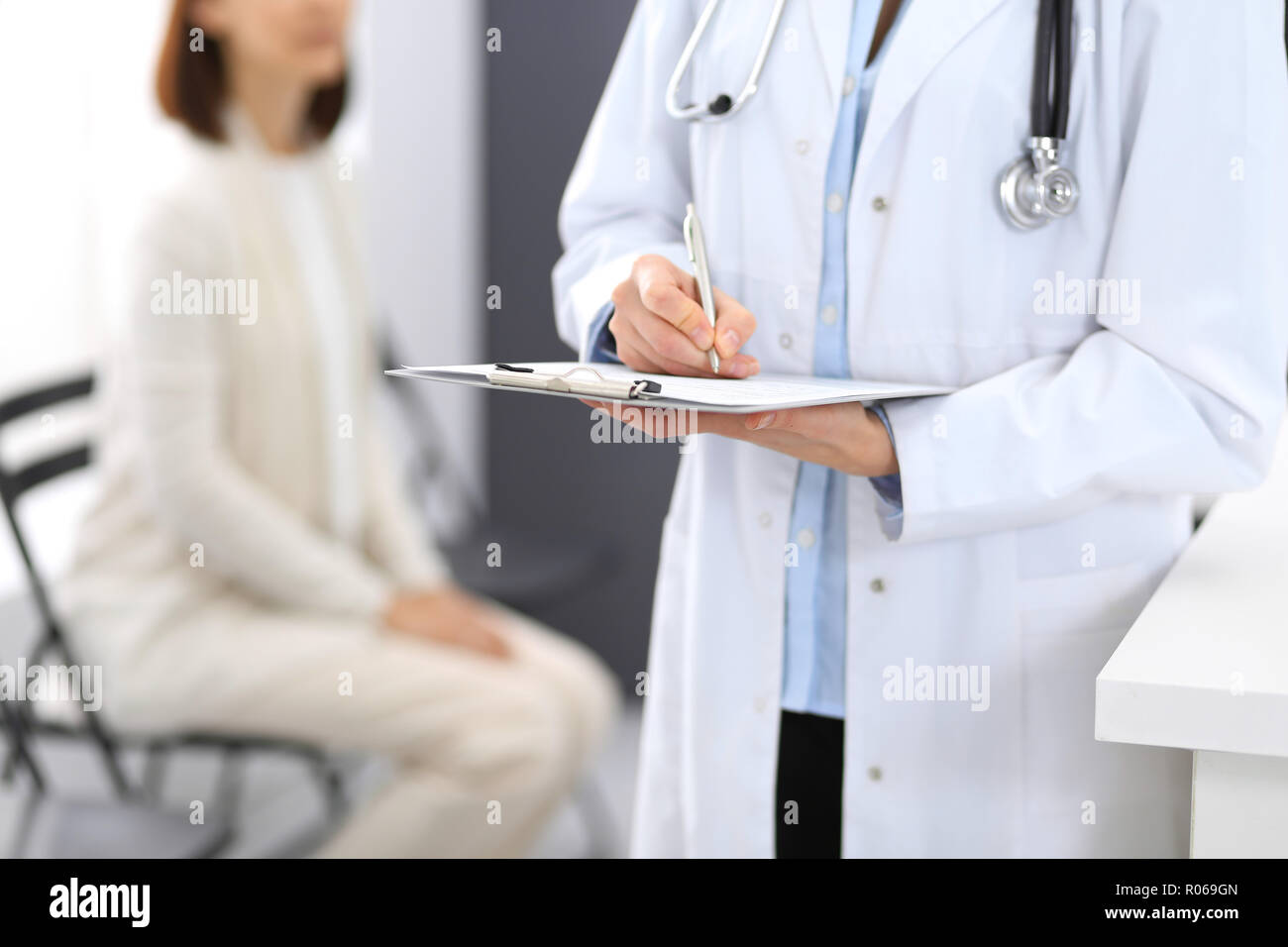 Doctor woman filling up medical form while standing near reception desk ...