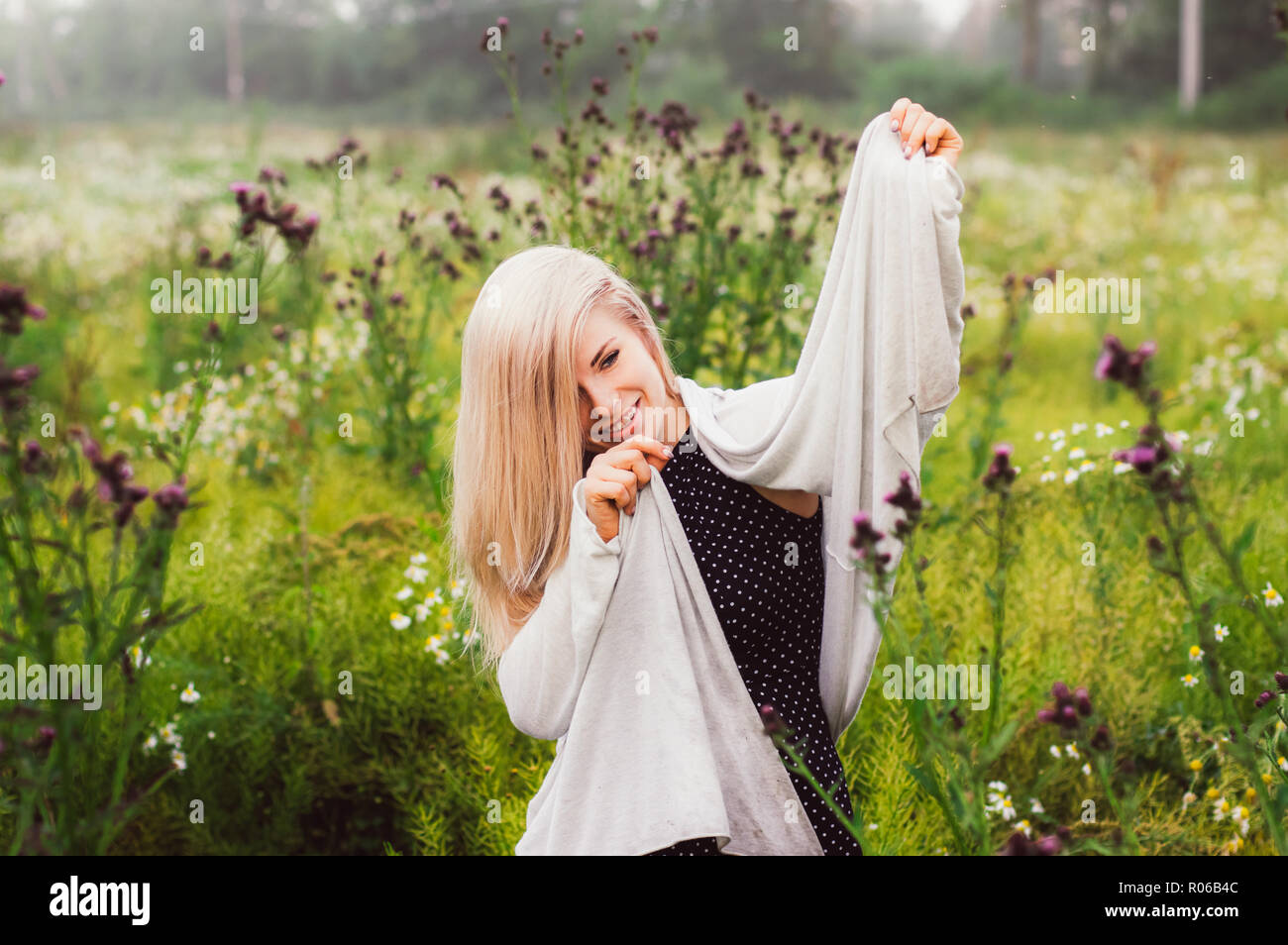 Portrait of smiling young girl dancing in chamomile field in sunrise, thistle on first plan ...