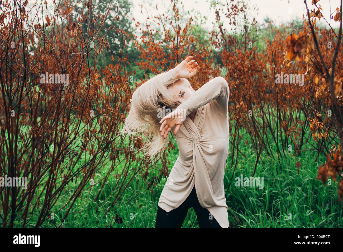 Portrait of young girl dancing between dead trees, in motion with hands ...
