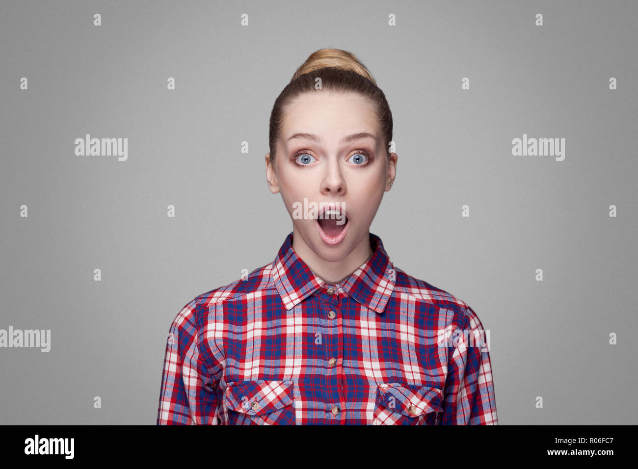 Amazed beautiful blonde girl with pink checkered shirt, collected bun ...