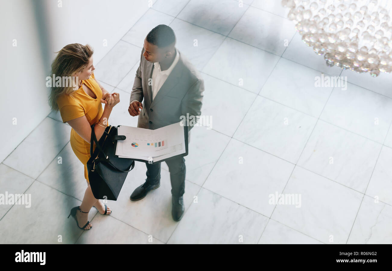 Two young business professionals standing together and discussing over ... Two young business professionals standing together and discussing over ...