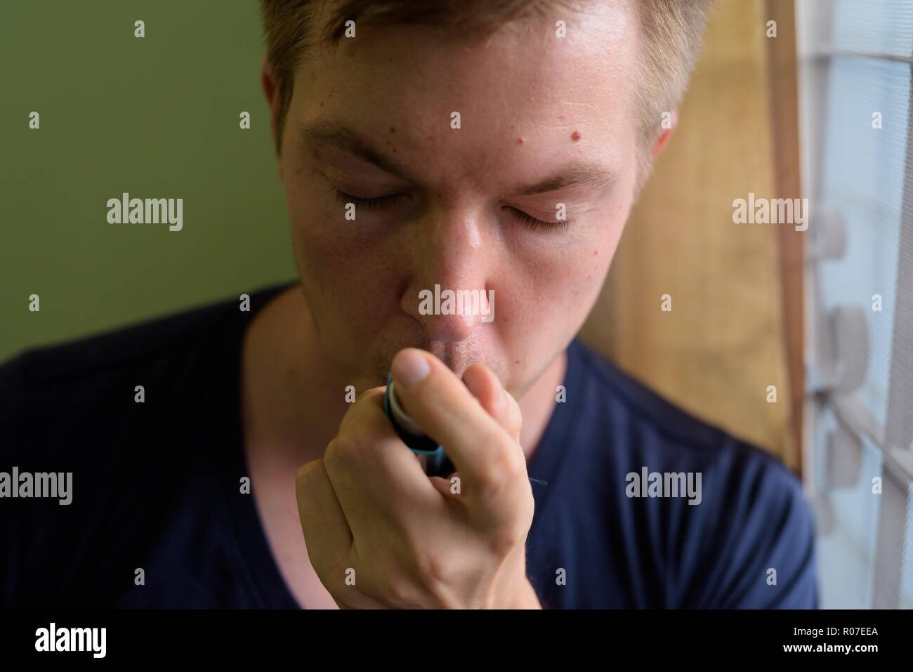 Young handsome man using asthma inhaler at home Stock Photo - Alamy