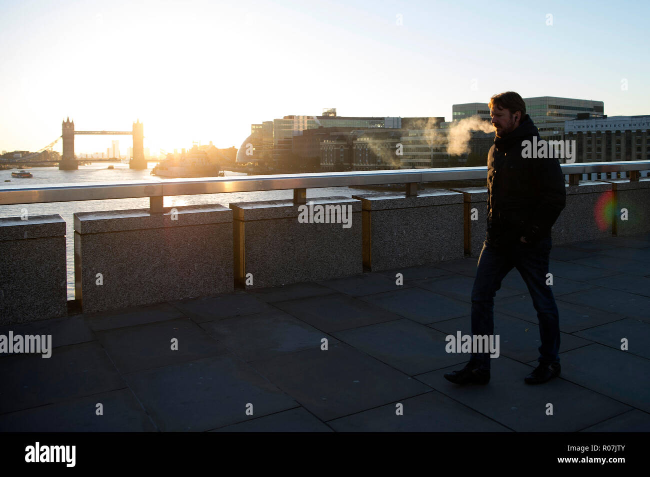 A commuter walks across London Bridge, with the sun rising behind Tower ...