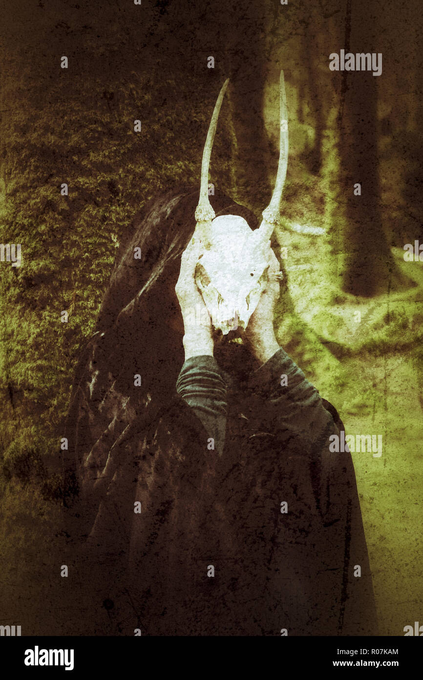 Female witch standing alone in dark woods holding a deer skull - John ...