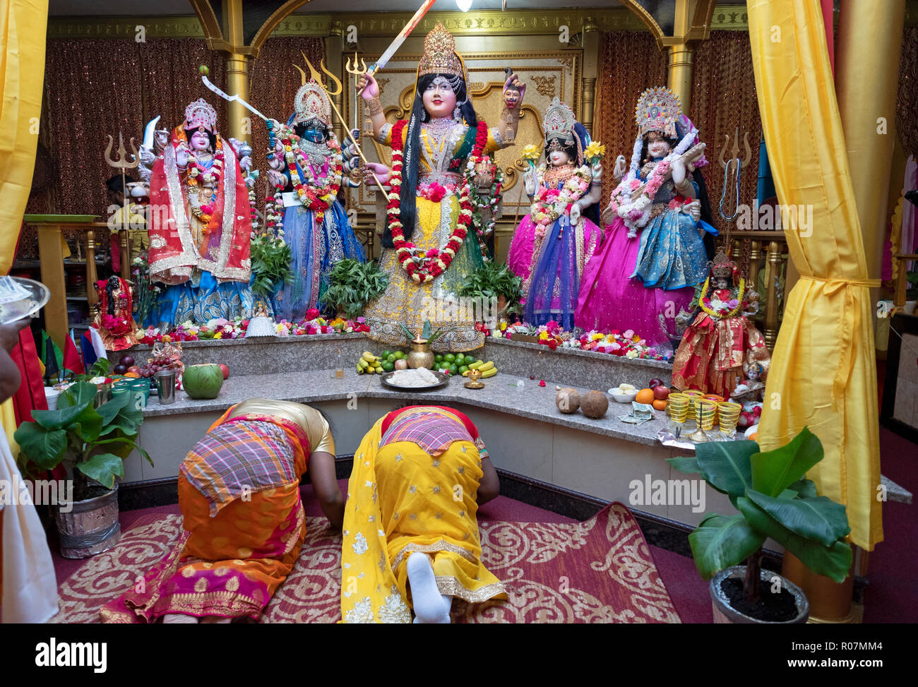 Two Hindu women bow in prayer & meditation in front of statues of ...