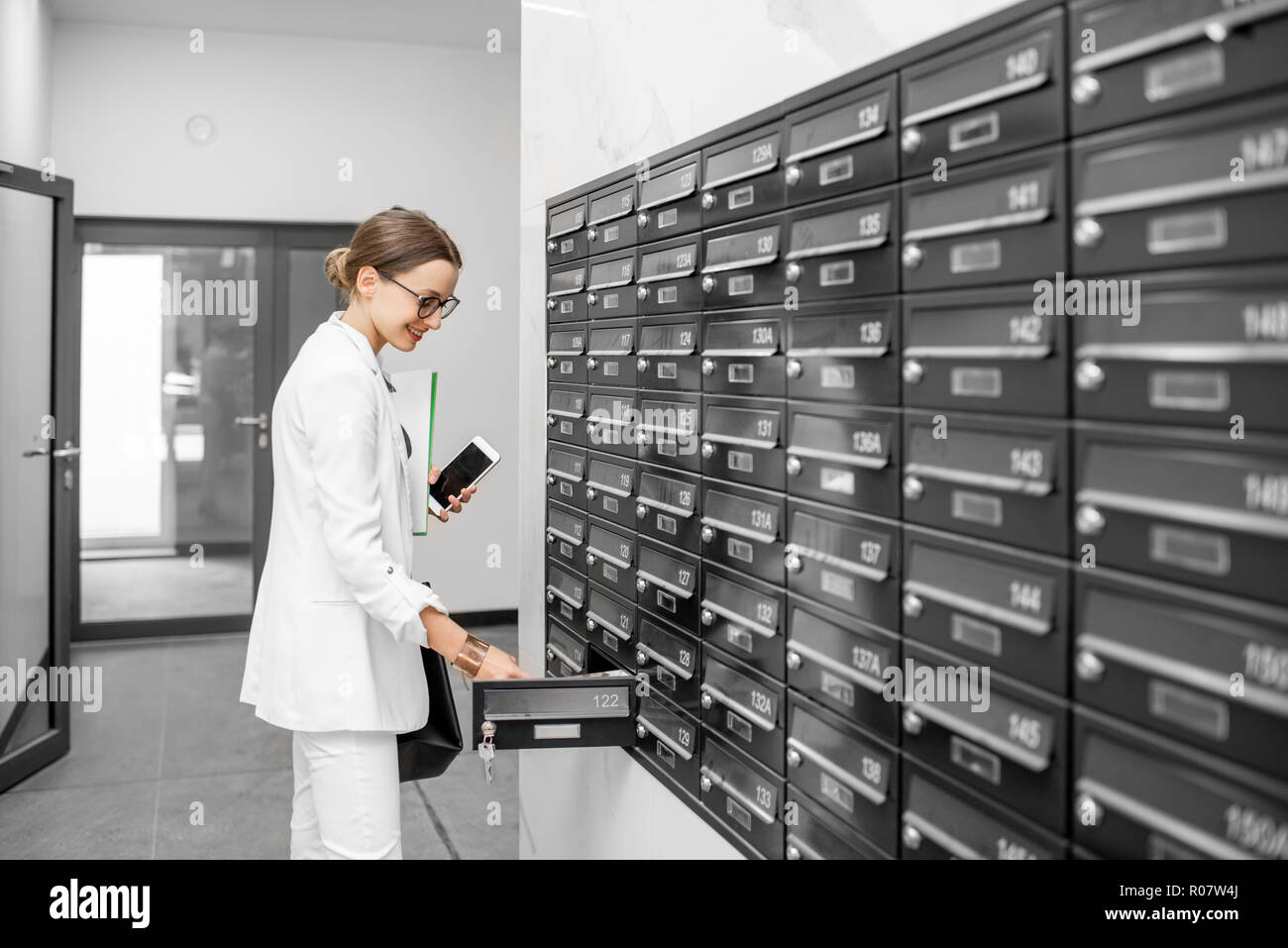 Happy business woman opening mailbox in the walkhall of the modern ...