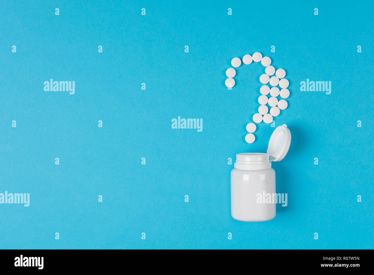 White pills in a question mark poured from a medicine bottle on blue ...
