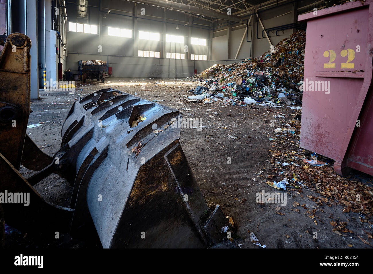 Heavy bulldozer bucket in rays of evening sun in building of waste ...