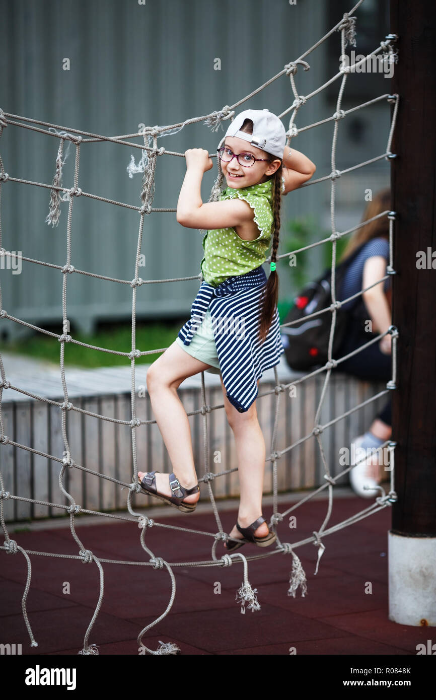 Happy girl on outdoor playground climbing frame. Child on rope climbing ...