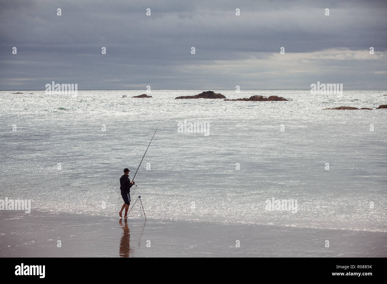 Man fishing from the beach in the Irish Sea on the coast of Anglesey ...