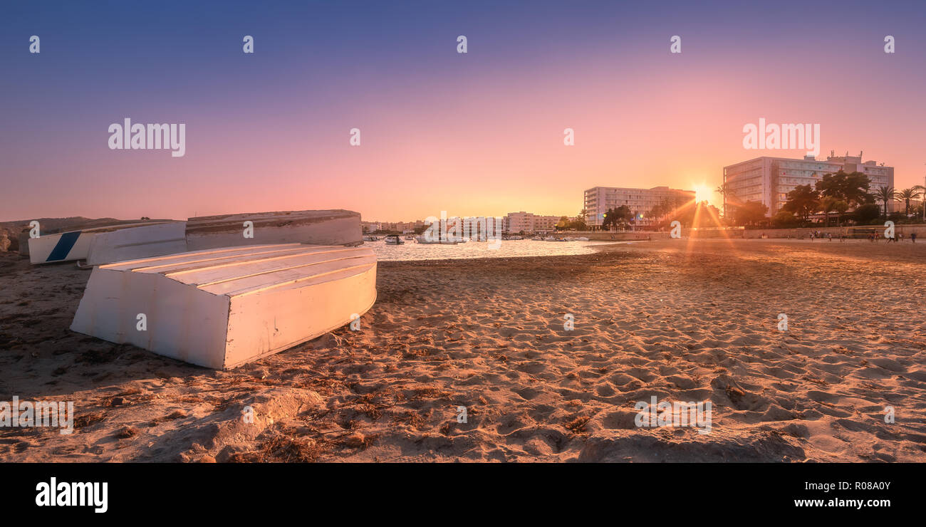 Sand shore with pastel sky, waves and sunbeams on stone during sunset ...
