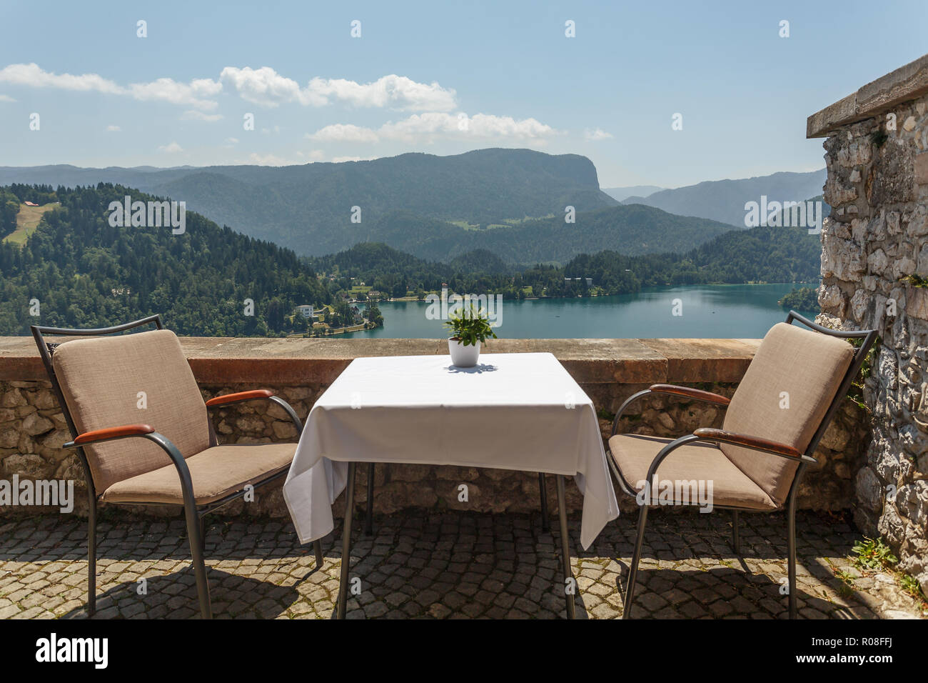 Tables and chairs of outdoor cafe. Views of the mountains and Lake Bled ...