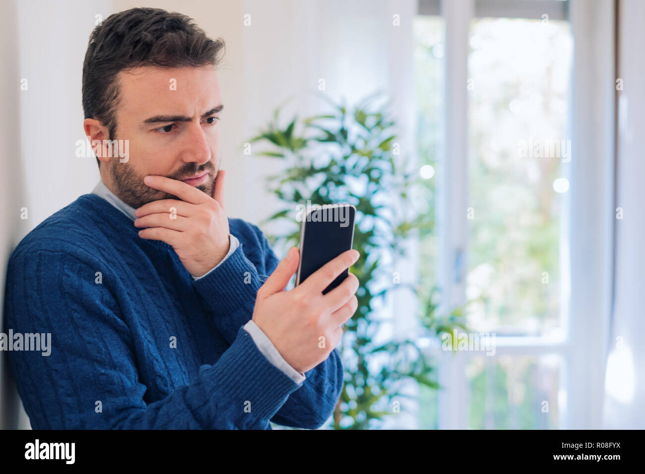 Thoughtful man watching his mobile phone Stock Photo - Alamy