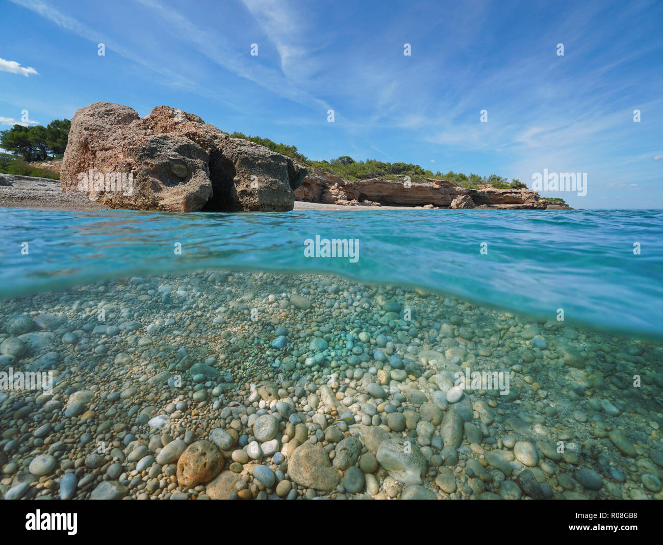 Pebble beach with rocky coast, split view half above and underwater ...
