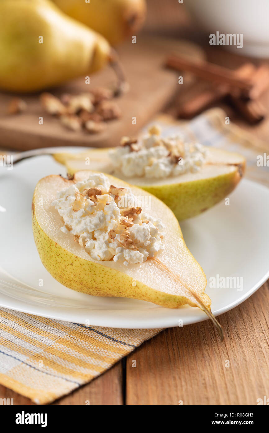 Half pears with cottage cheese and nuts on white dish. Wooden table ...