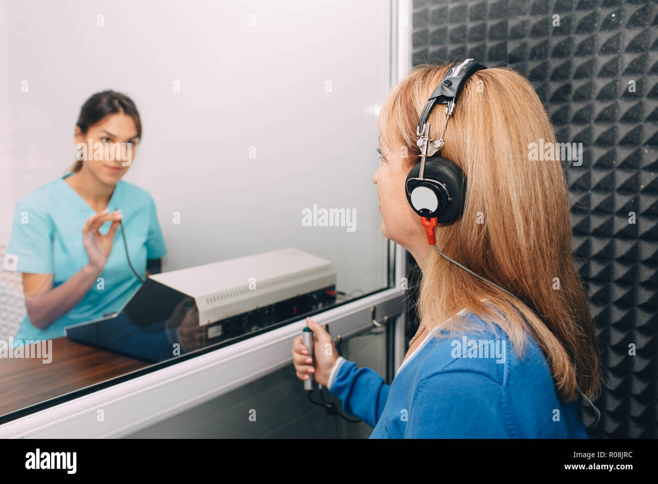audiologist doing hearing exam to a mature patient using audiometer in ...