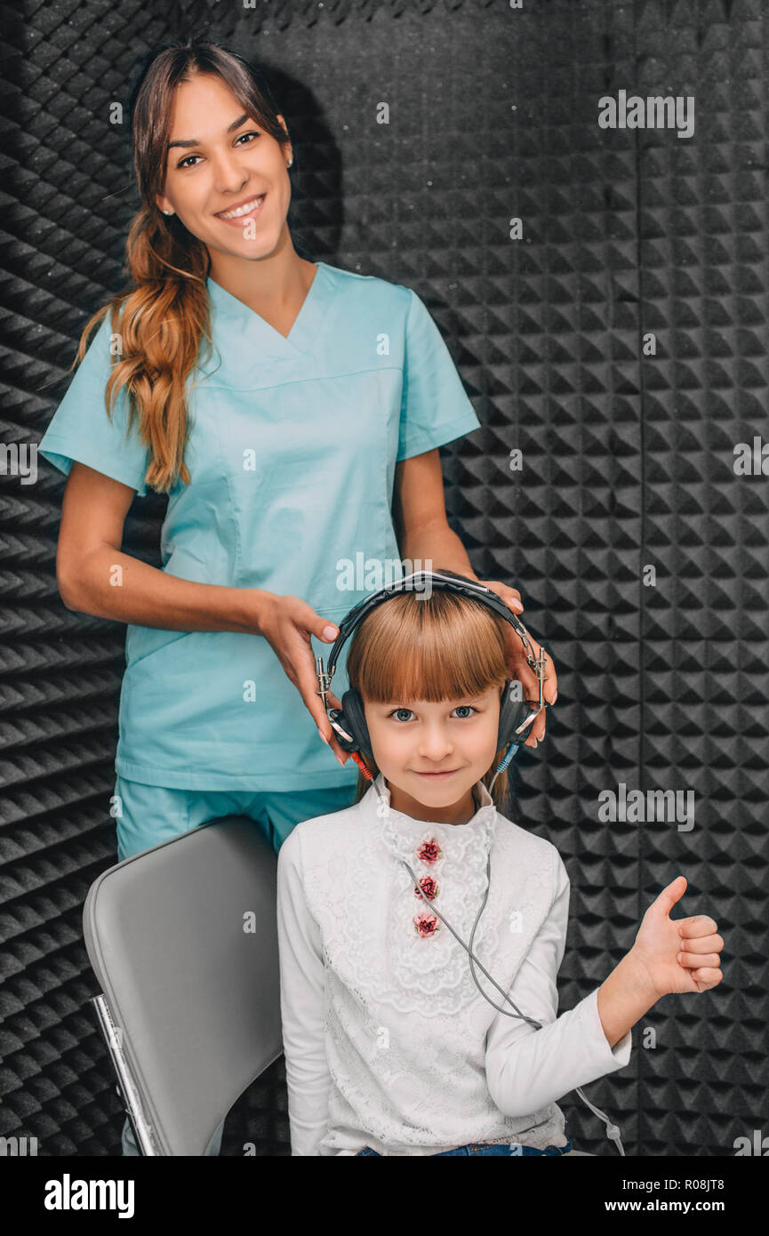 audiologist doing hearing exam to a little girl using audiometer in ...