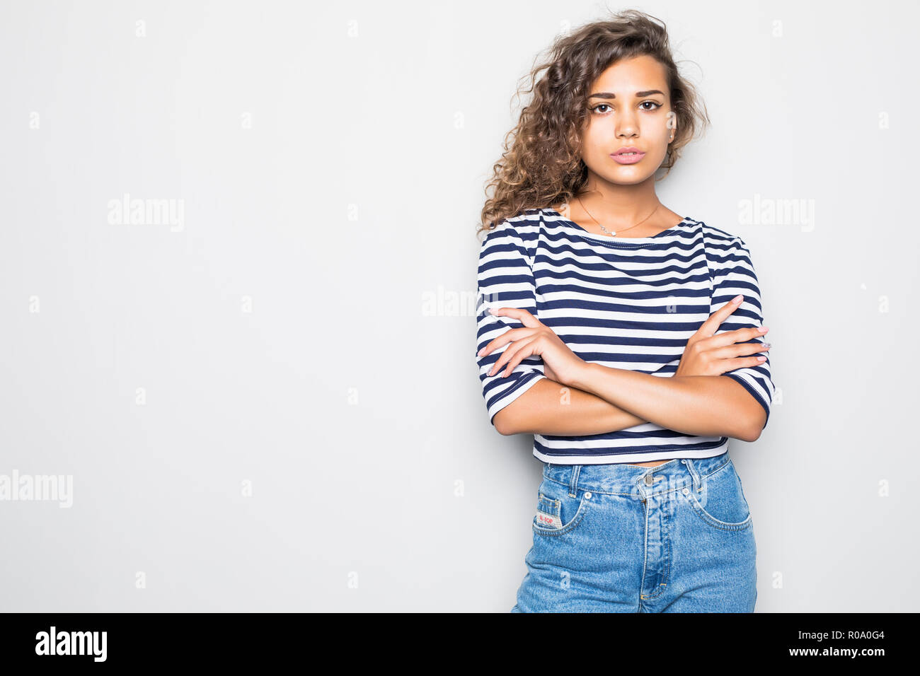 Portrait of cheerful curly mulatto woman holding hands crossed looking ...