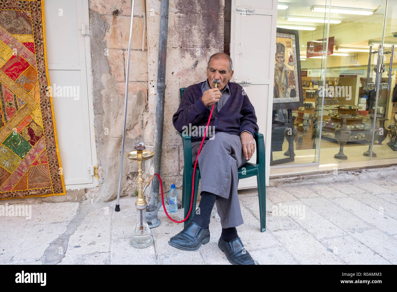 An Arabic man smoking a hookah outside of his shop in the Muslim ...