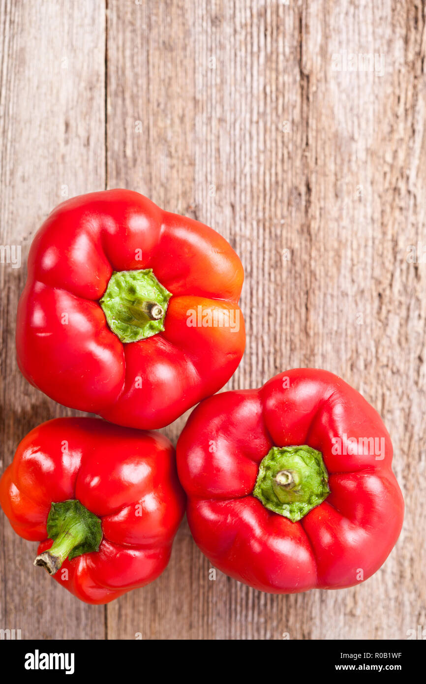 three red bell peppers on rustic wooden table Stock Photo - Alamy