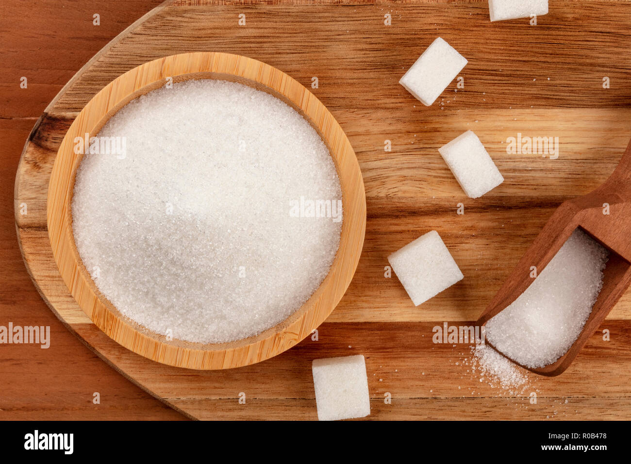 A closeup photo of a bowl and a scoop of white sugar, with sugar cubes ...