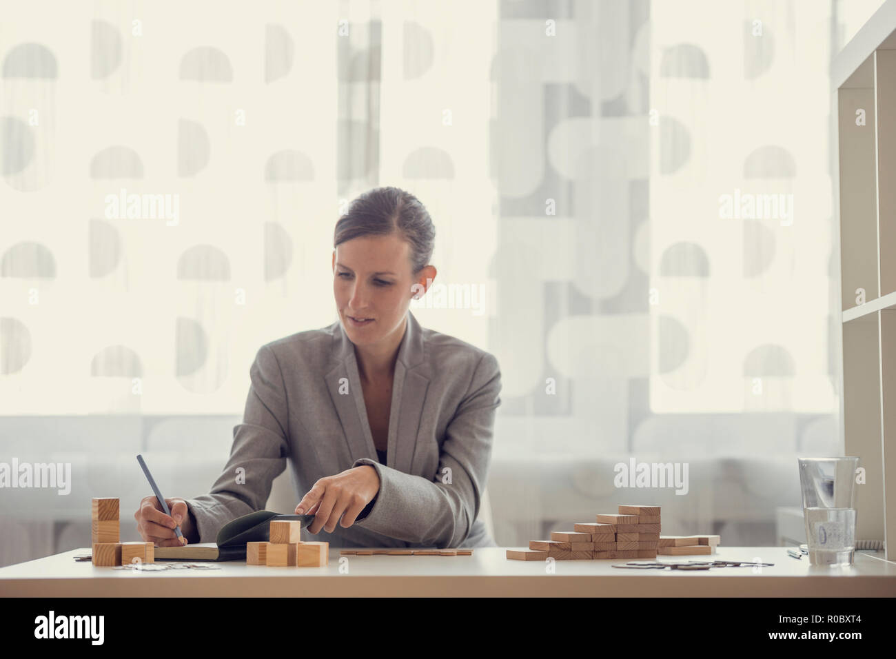 Businesswoman working at office desk writing on notepad beside stacks ...