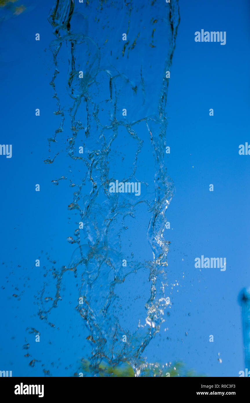 transparent falling water vertical flows against a blue sky and green ...