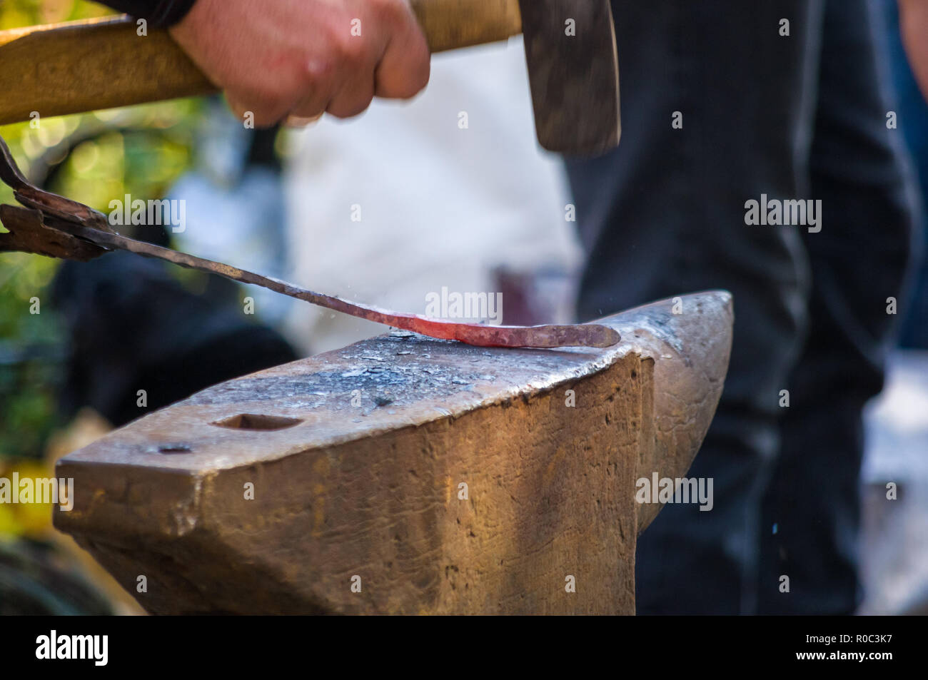 blacksmith performs the forging of hot glowing metal on the anvil ...