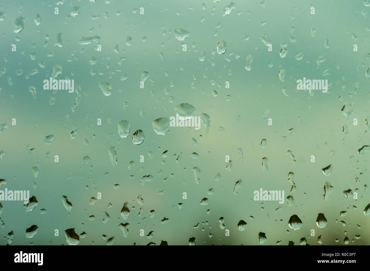 raindrops on window glass on background of cloudy sky and landscape ...