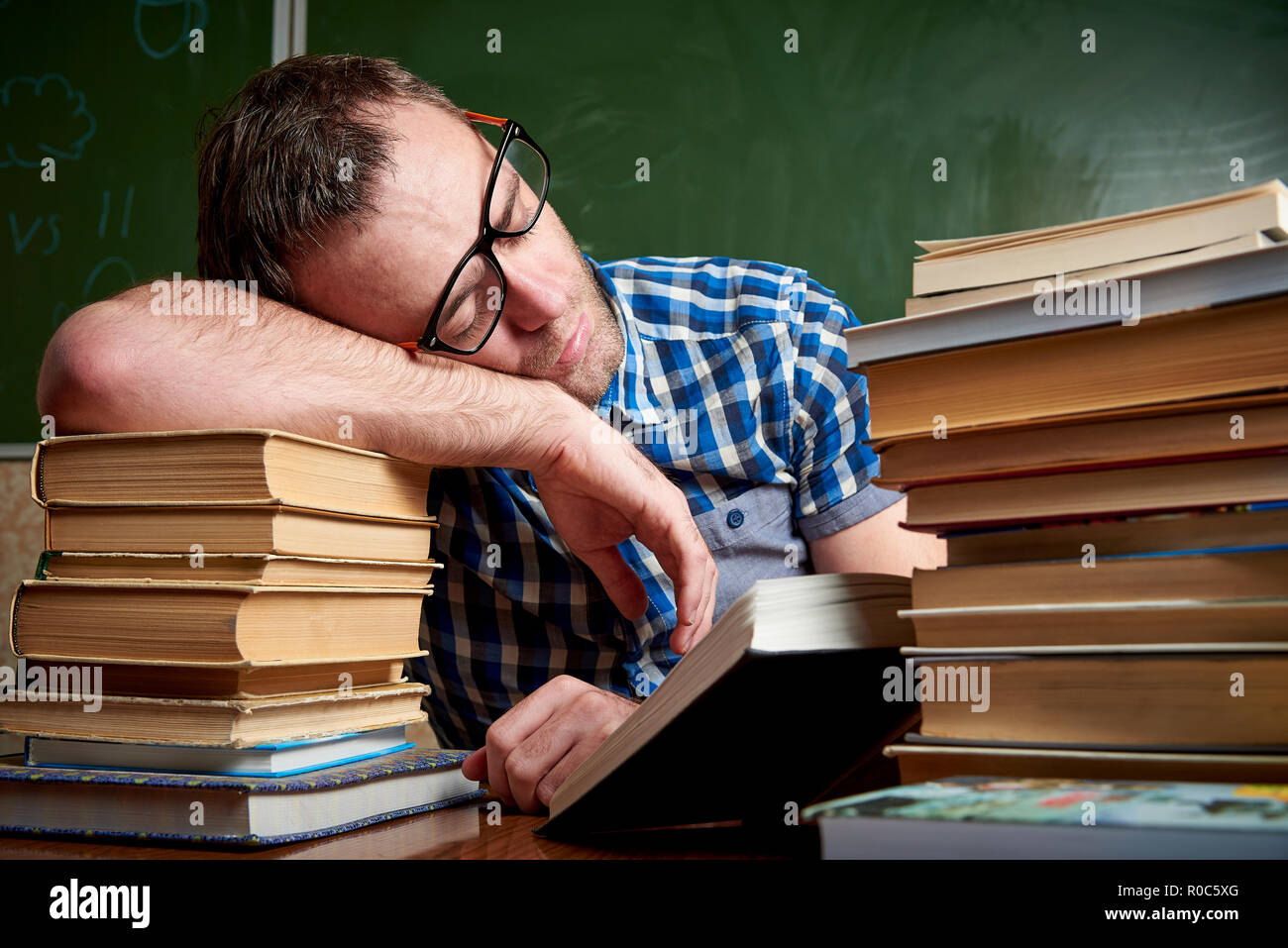 Tired and tortured disheveled student in glasses is sleeping at the ...