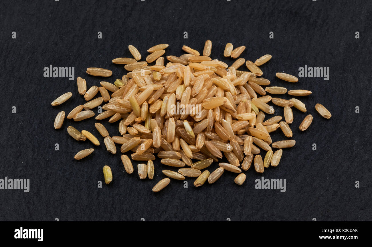 Brown rice groats on black background Stock Photo - Alamy