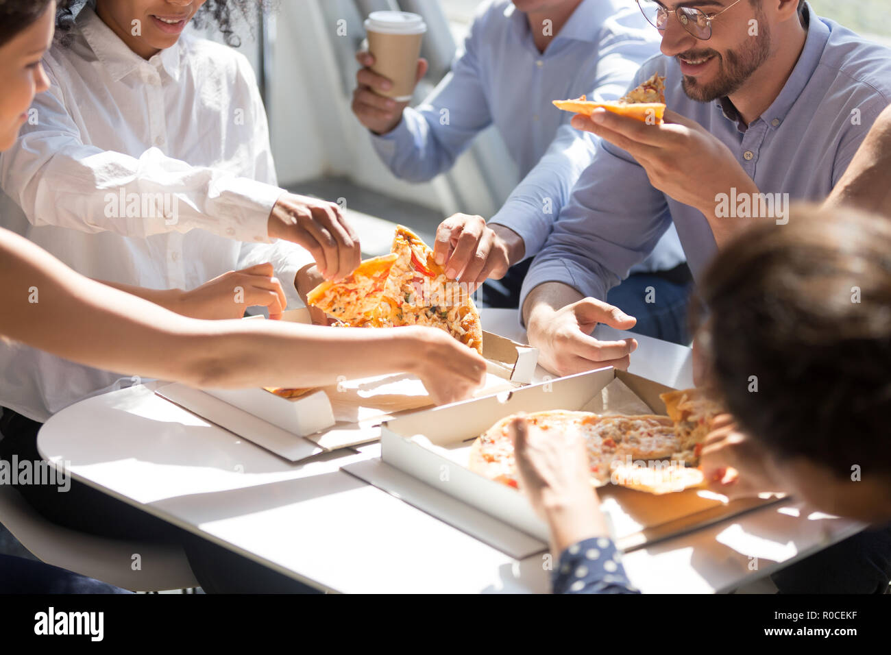 Diverse workers taking pizza from box on table eating together Stock ...