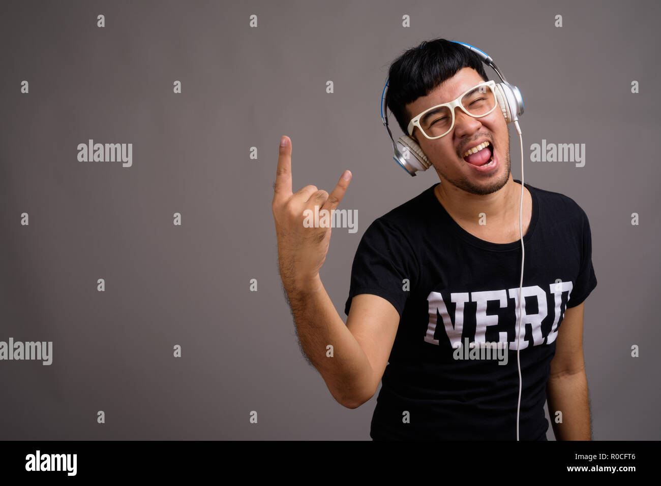 Young Asian nerd man listening to music against gray background Stock ...