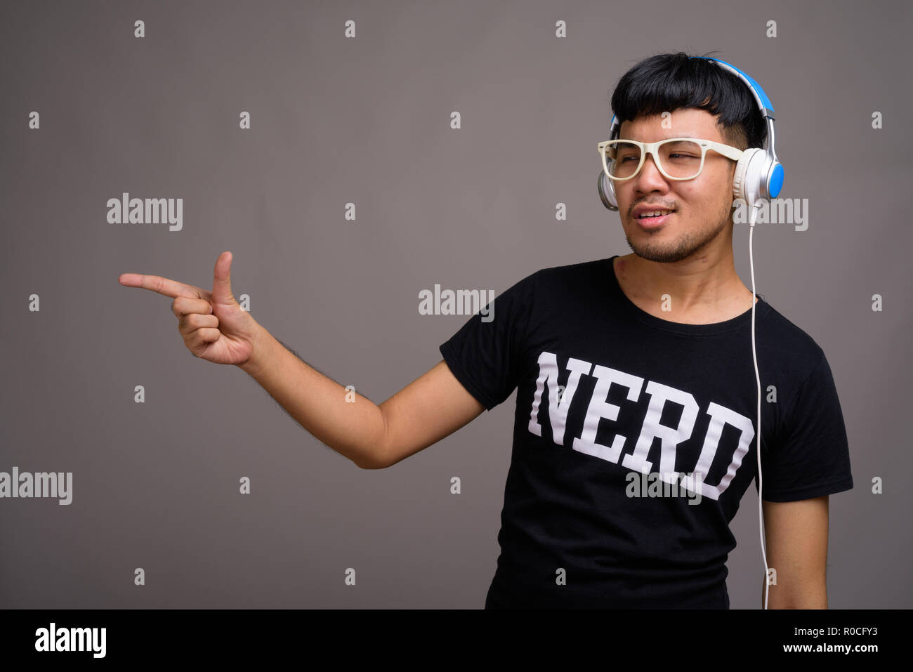 Young Asian nerd man listening to music against gray background Stock ...