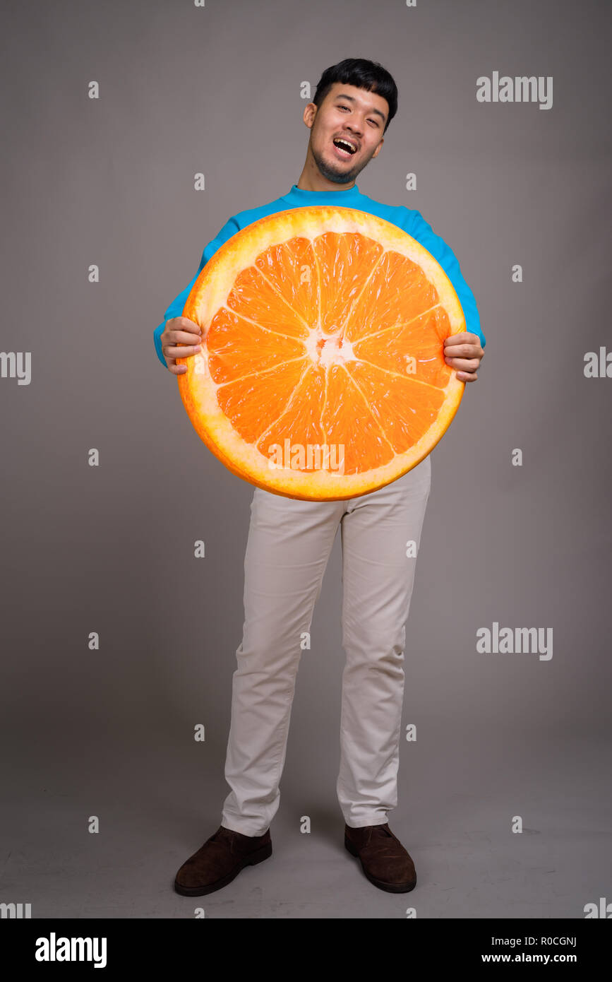Portrait of young Asian man holding big slice of orange Stock Photo - Alamy