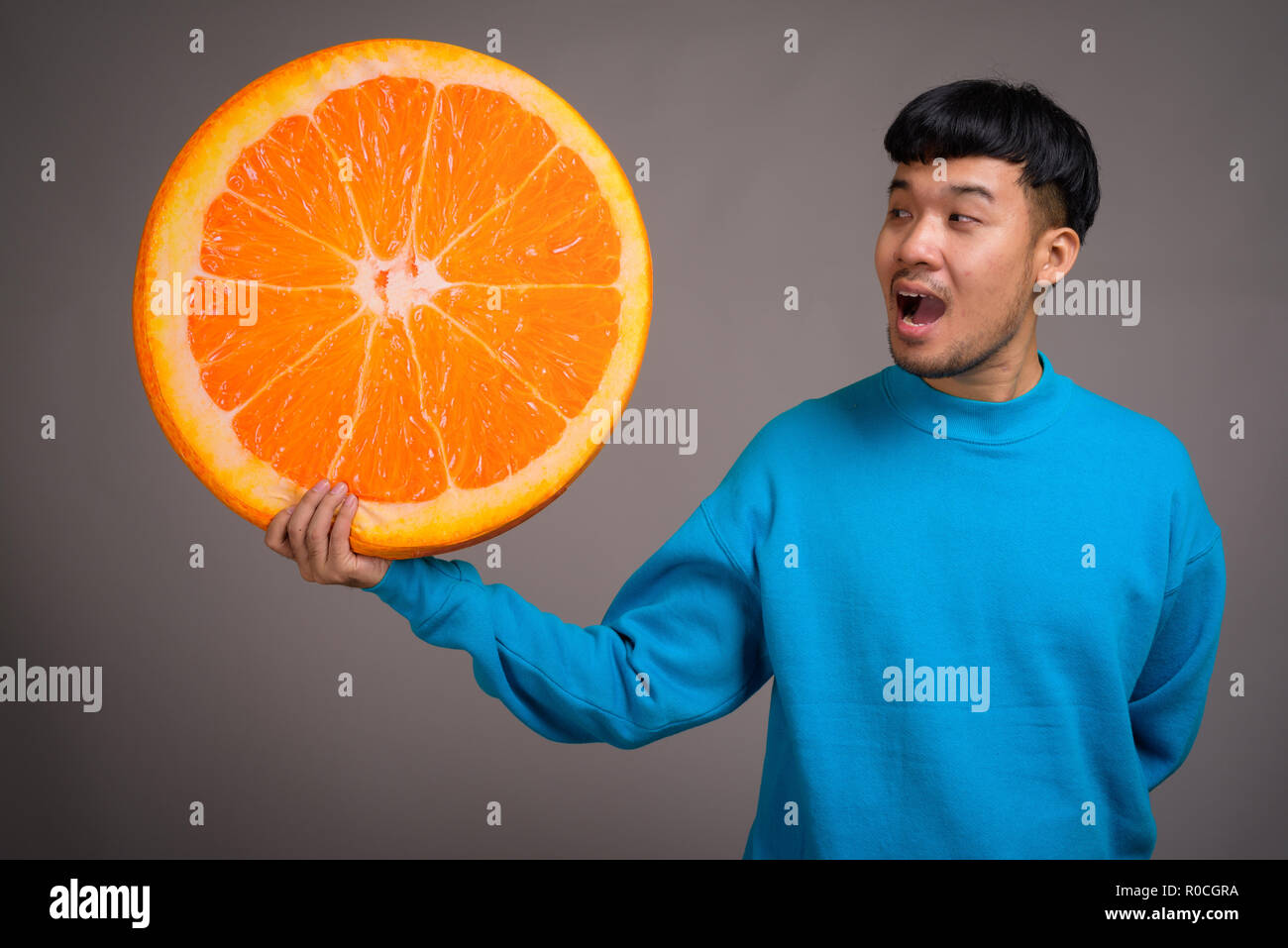 Portrait of young Asian man holding big slice of orange Stock Photo - Alamy