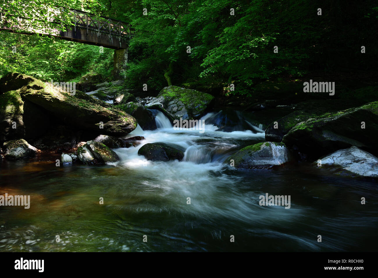 Long exposure of a waterfall flowing under a bridge at Watersmeet in ...