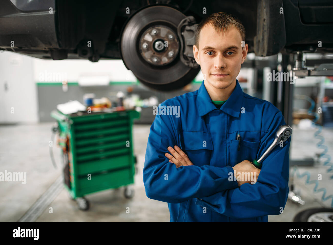 Repairman with wrench against a car on the lift, suspension diagnostic ...