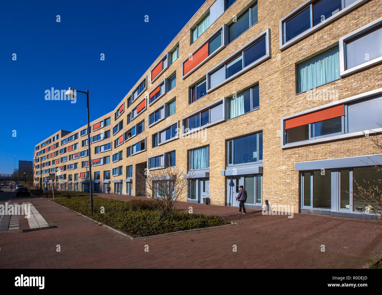Modern apartment building with light bricks and orange sun screens in a ...