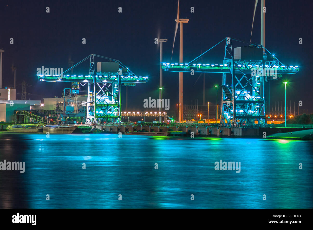 Wharf during twilight with huge modern cranes under colorful lighting ...