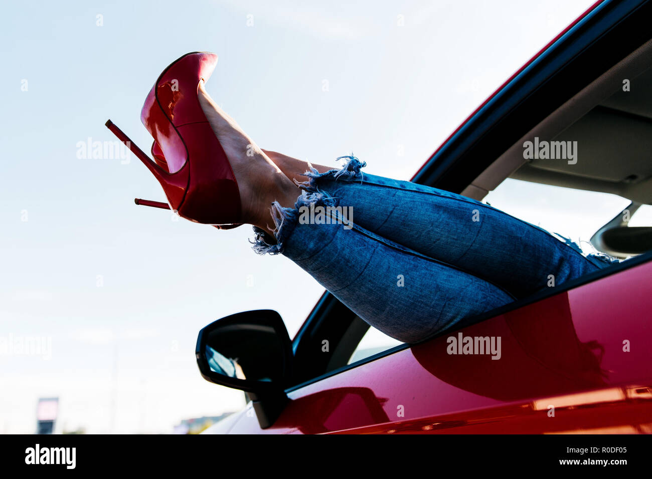 Image of woman's legs in red shoes and jeans protruding from red car ...