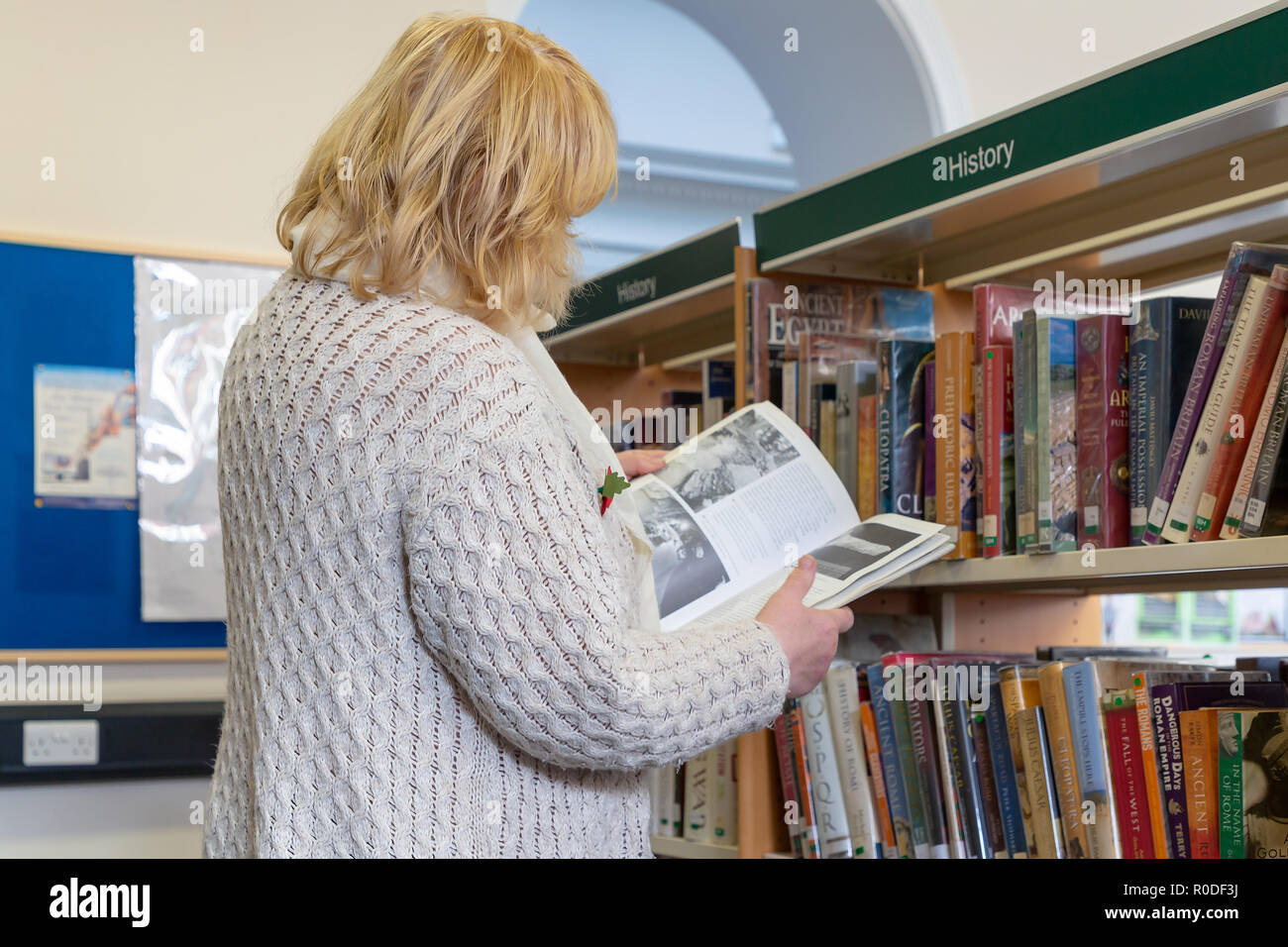 Mature, blond lady looking through the books in the history section of ...