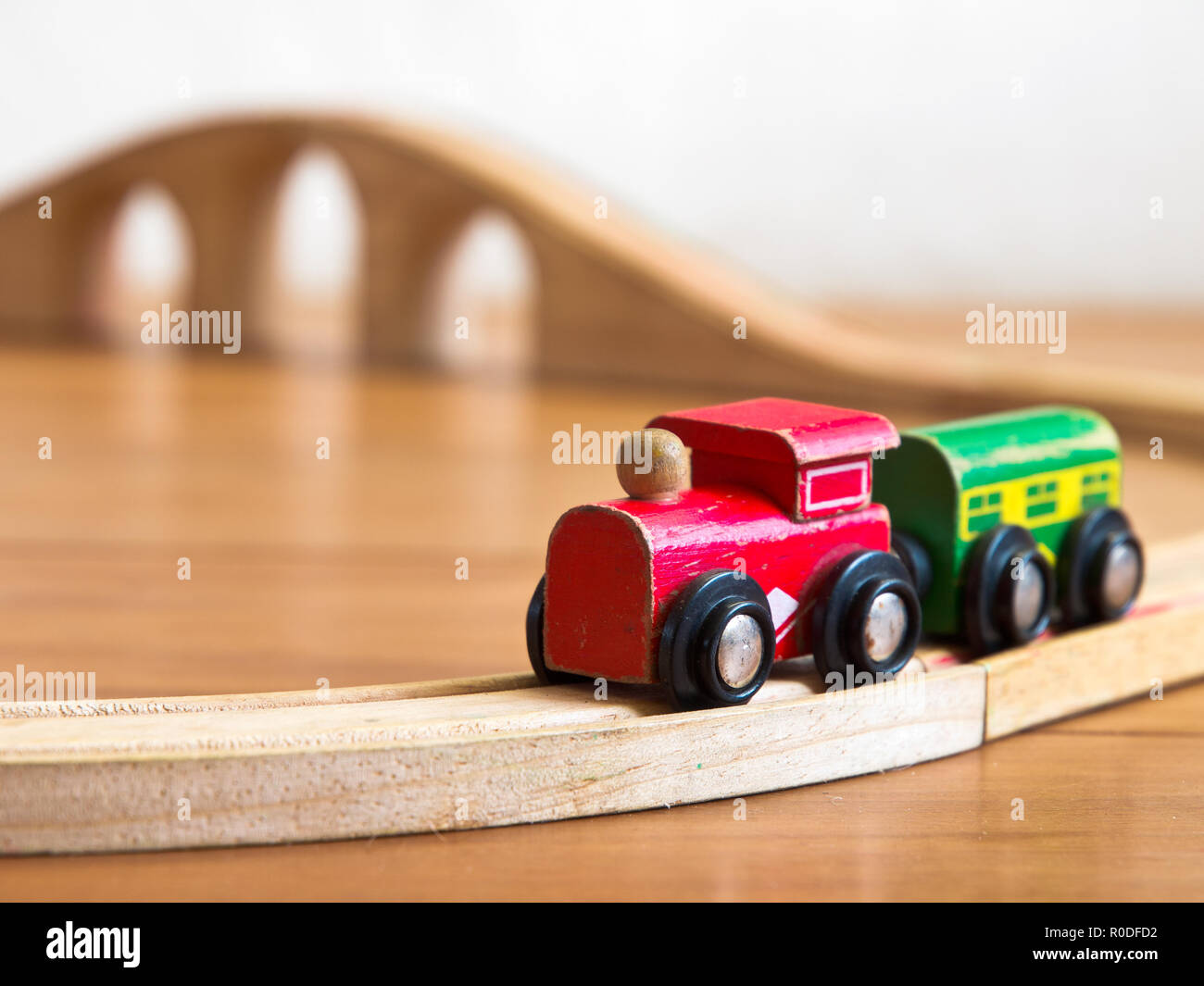 Red and green wooden toy train on railroad with bridge in backdrop ...