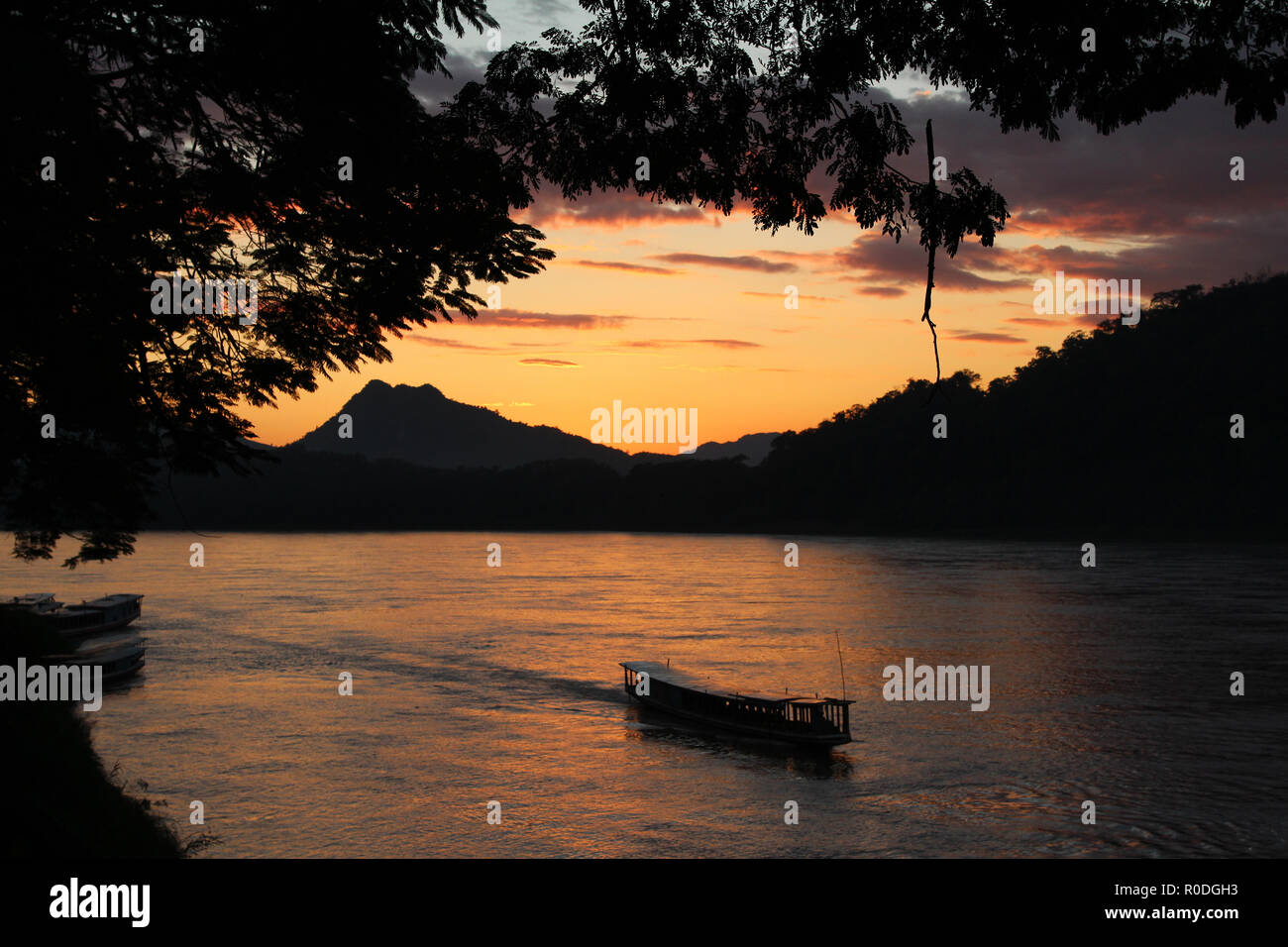 Orange sunset reflected on the Mekong River, with cruise boat and ...