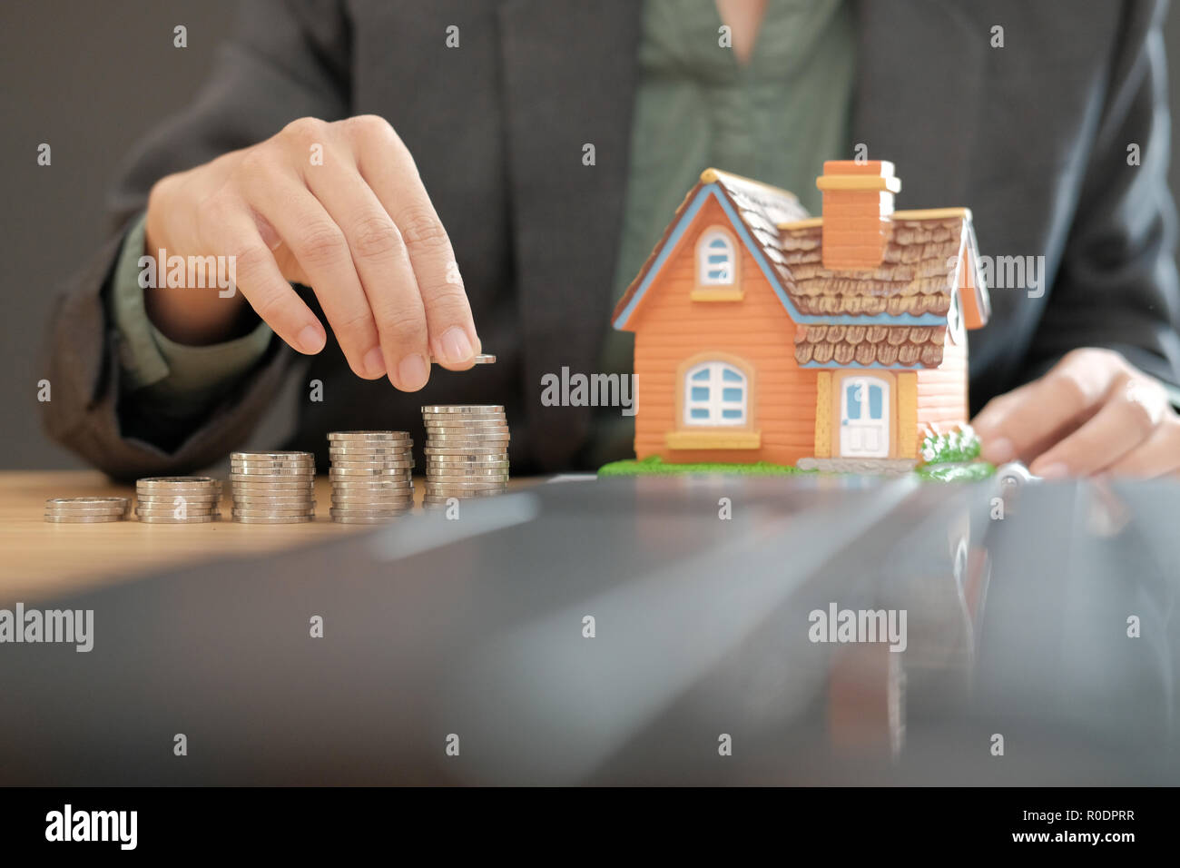 hand putting coins on stack with house model. saving money for buying ...